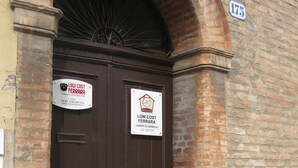 Uma porta dupla de madeira com duas placas, uma para 'Low Cost Ferrara' e outra para 'Low Cost Ferrara Camera Economiche'.