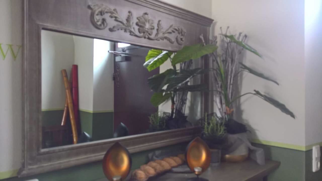 Um espelho com moldura decorativa, um vaso de planta e um tabuleiro de madeira com dois castiçais.
