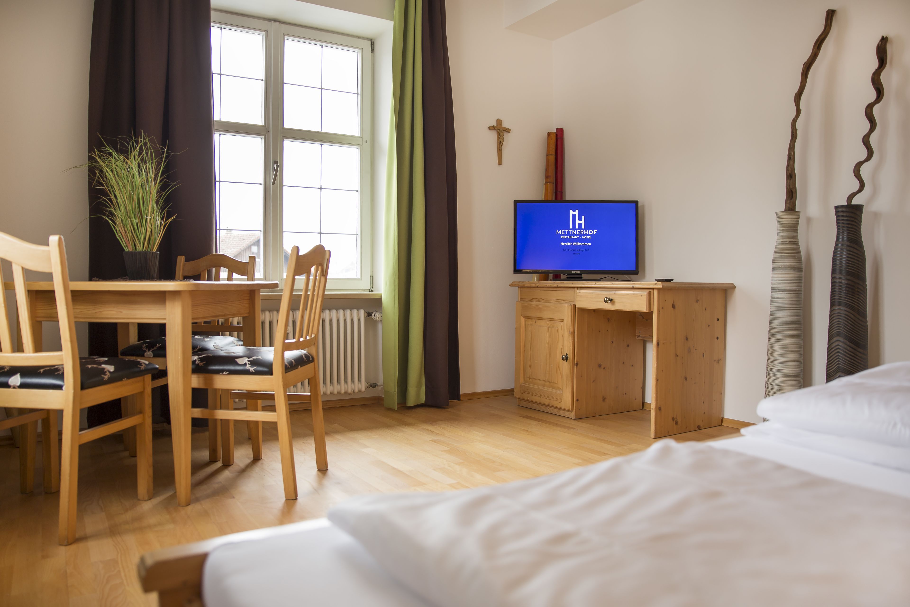 Quarto de hotel com escrivaninha de madeira, televisão, cama e janela com cortinas.