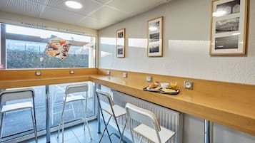 Cozinha moderna com bancada de madeira, cadeiras brancas e vista pela janela.