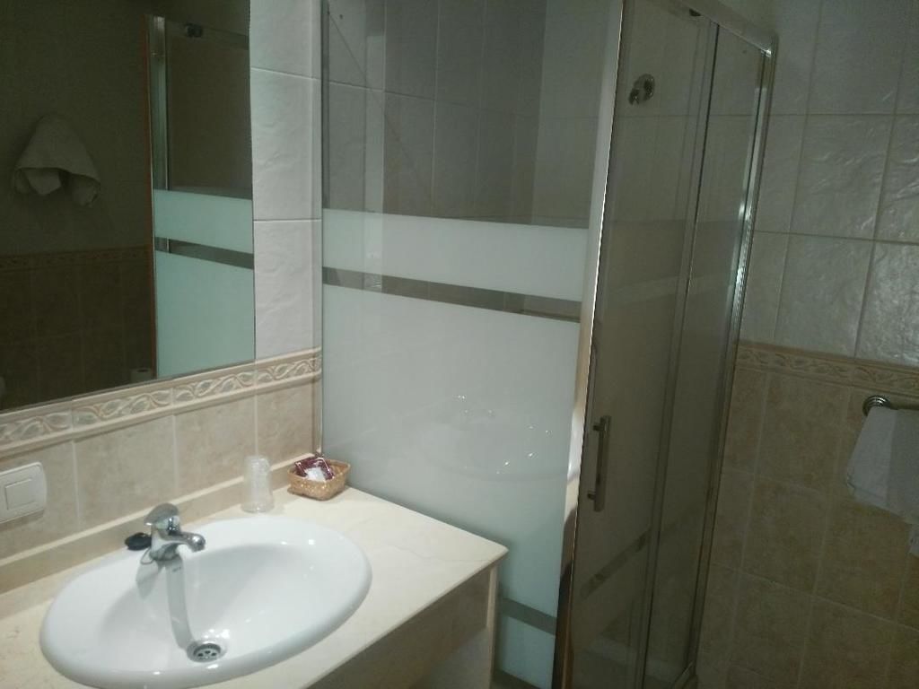 Casa de banho com lavatório, espelho e cabine de duche em vidro.