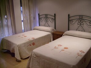 Duas camas de solteiro com colchas florais em um quarto com assoalho de madeira e uma mesinha de cabeceira entre elas.