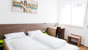 Quarto de hotel com duas camas, uma escrivaninha, uma cadeira, uma mesinha e um quadro na parede.