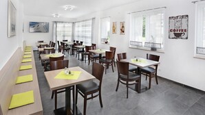 Uma sala de jantar moderna com várias mesas e cadeiras, um longo banco com jogos americanos amarelos, e uma parede com um letreiro com tema de café.