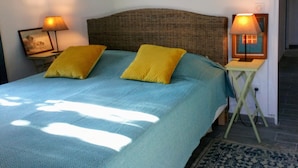 Uma cama com colcha azul e duas almofadas amarelas, com duas mesas de cabeceira de cada lado, cada uma com uma luminária.