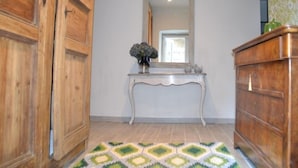 Um corredor com porta de madeira, mesa consola com um vaso, um espelho e cómoda de madeira.
