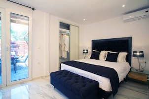 Um quarto moderno com uma cama grande, uma porta de vidro que dá para uma área externa e uma mesa de cabeceira com abajur.