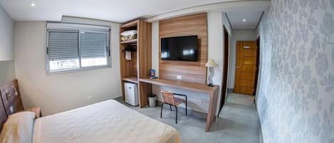 Um quarto com cama, escrivaninha, cadeira, televisão e guarda-roupa.