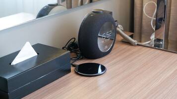 Uma mesa de madeira com um alto-falante preto, um smartphone e uma caixa de lenços.