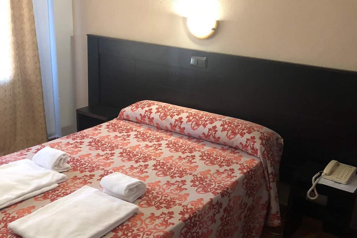 Quarto de hotel com cama, mesa de cabeceira e telefone fixo na parede.