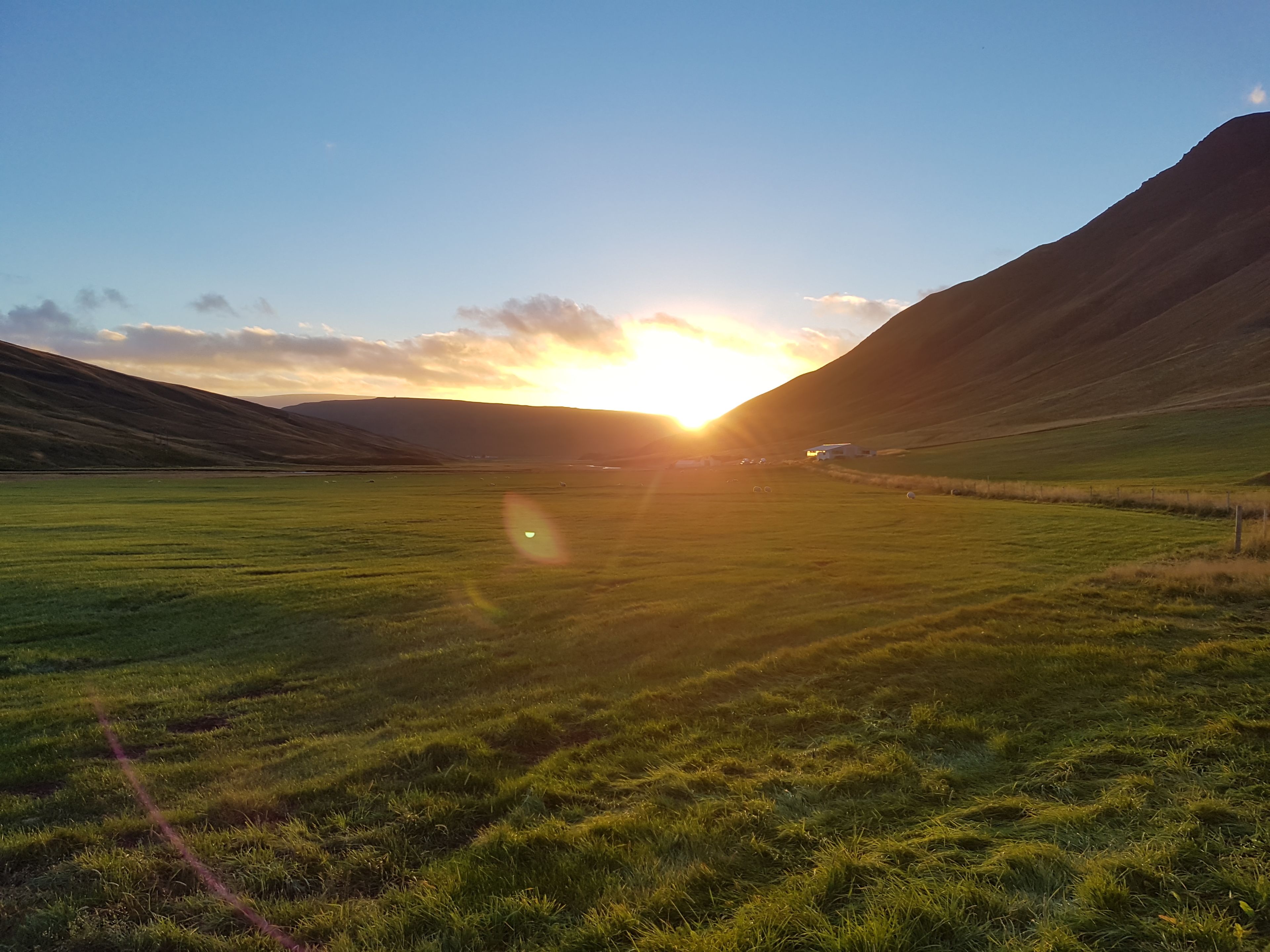 Um campo amplo com um pôr do sol ao longe, rodeado por colinas.