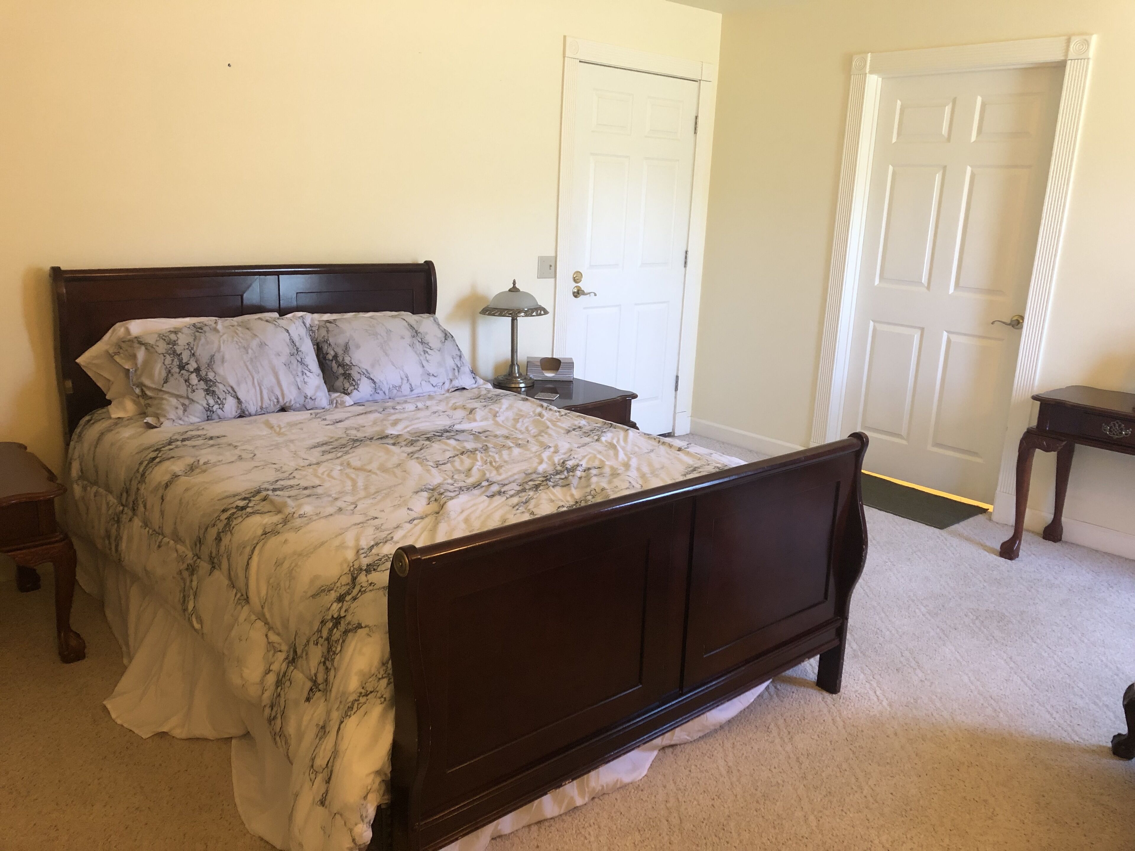 Quarto com cama, mesas de cabeceira, abajur e porta.