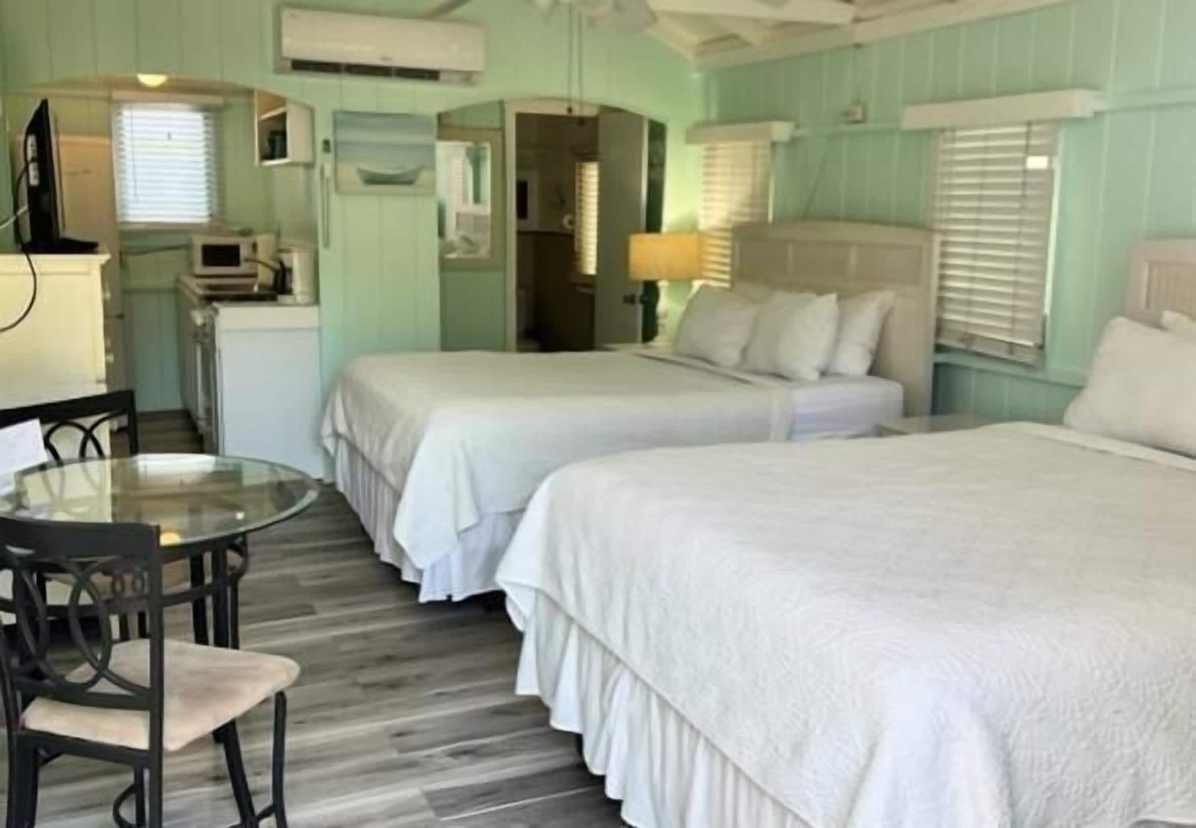 Quarto de hotel com duas camas, uma mesa pequena com uma cadeira, uma escrivaninha com um computador e um espelho.