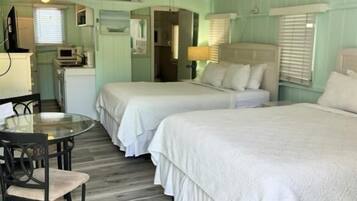 Quarto de hotel com duas camas, uma mesa pequena com uma cadeira, uma escrivaninha com um computador e um espelho.