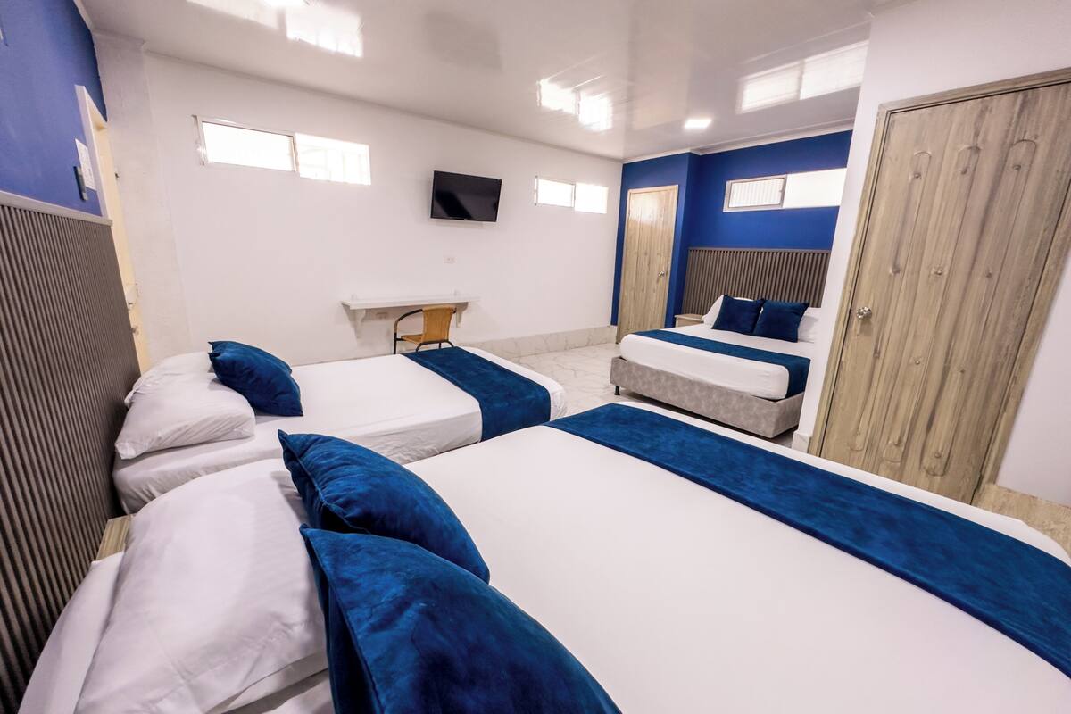 Quarto de hotel com três camas, uma televisão fixada na parede e um guarda-roupa de madeira.