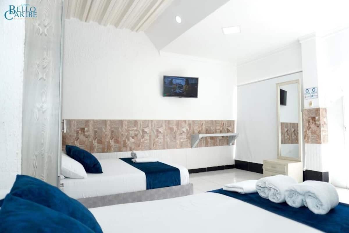 Quarto de hotel com uma cama grande, televisão presa na parede e banheiro com espelho e porta-toalhas.