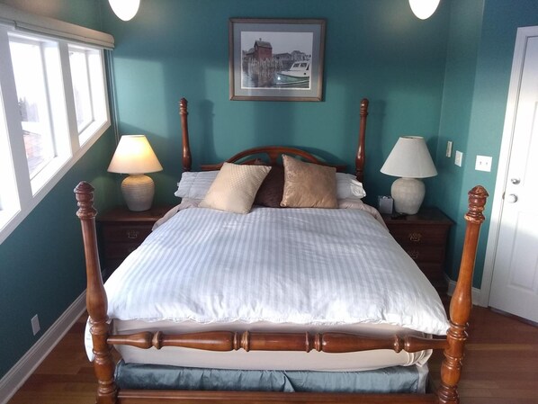 Uma cama bem arrumada com estrutura de madeira, duas mesas de cabeceira com luminárias e um quadro na parede.