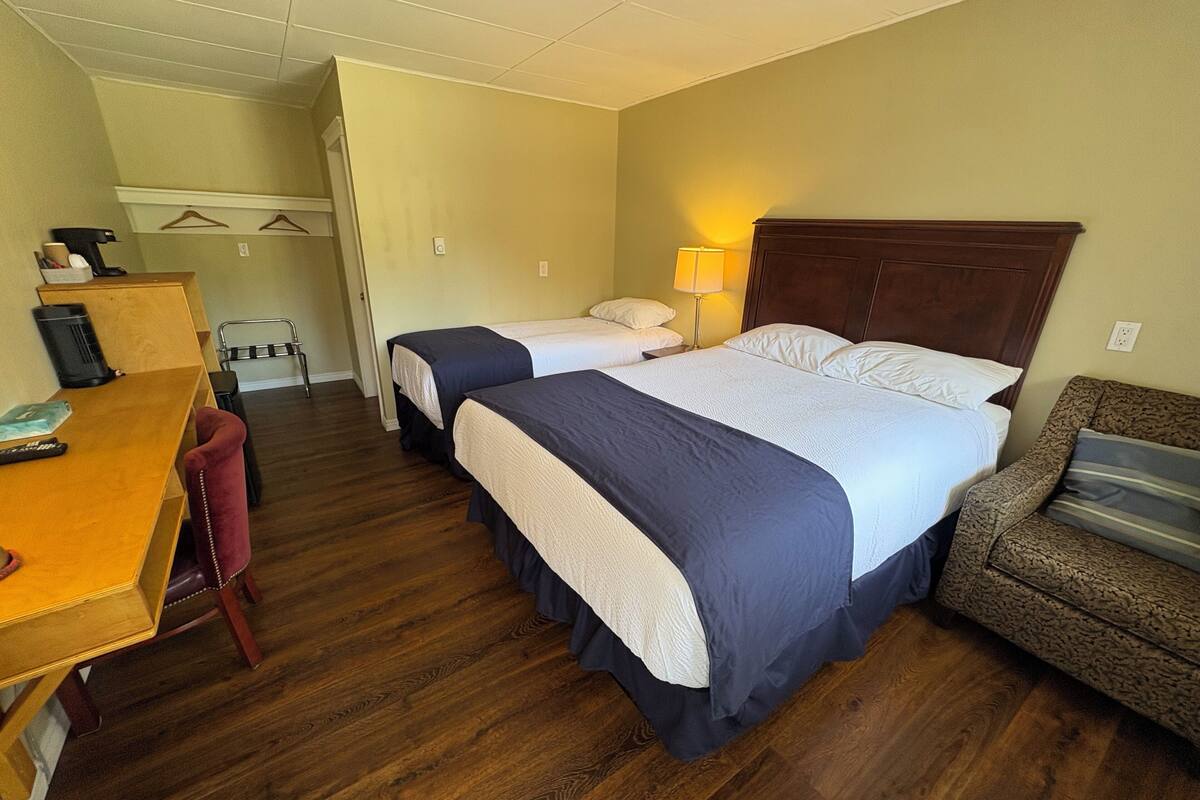 Quarto de hotel com duas camas, uma escrivaninha, uma cadeira e um sofá.