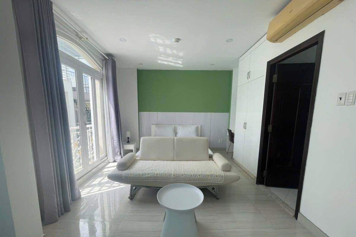 Quarto moderno com uma cama grande, uma mesinha redonda e vista para o exterior através de uma janela ampla.