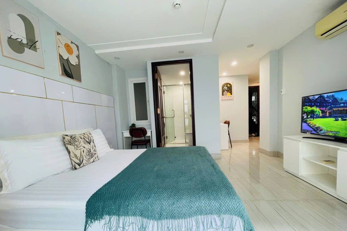 Quarto moderno com uma cama, televisão e um banheiro visível ao fundo.