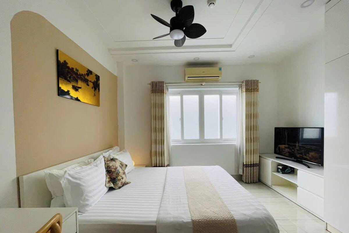 Quarto de hotel com cama, escrivaninha, televisão e ventoinha no teto.