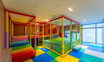 Uma área de recreação infantil com piso acolchoado colorido, escorrega e estruturas de brincadeira fechadas.