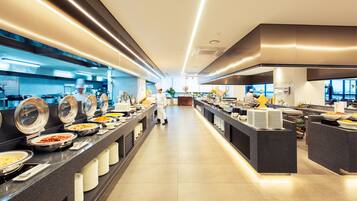 Buffet moderno com diversas estações de comida, um chef de uniforme e ambiente limpo e bem iluminado.