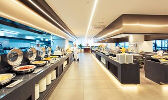 Buffet moderno com diversas estações de comida, um chef de uniforme e ambiente limpo e bem iluminado.