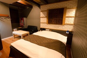 Quarto de hotel com uma cama grande, uma mesa pequena, um banco e um painel decorativo na parede.