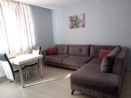 Uma sala de estar com um sofá marrom, uma mesa de jantar branca e um quadro na parede.