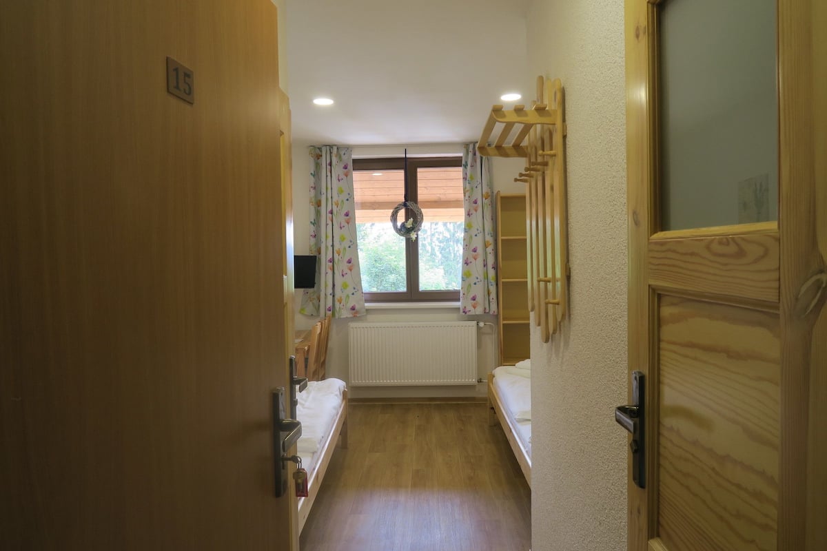 Um corredor estreito com piso de madeira, uma janela com cortinas florais e um radiador.