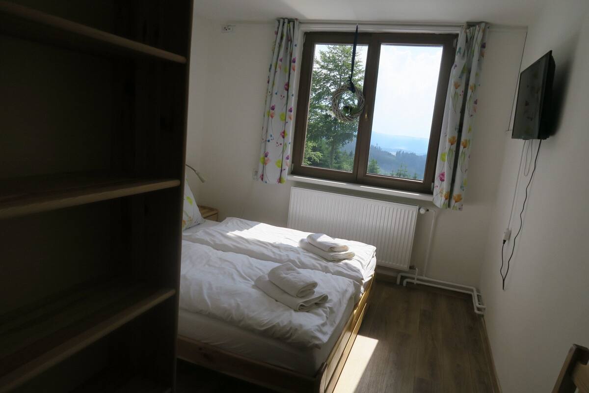 Quarto com cama, janela com cortinas, radiador e televisão na parede.