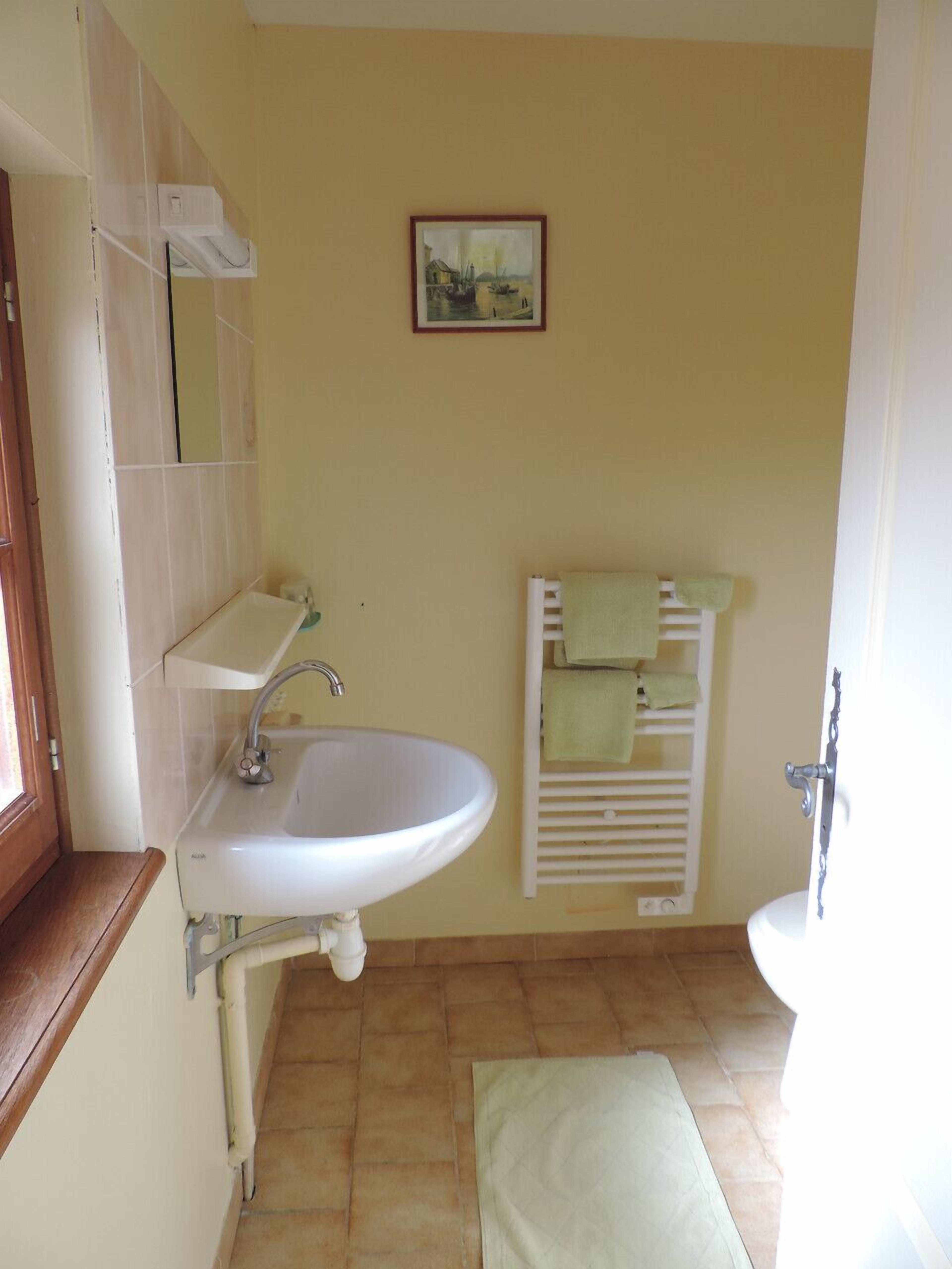 Uma casa de banho com uma pia branca, um espelho, um porta-toalhas e um quadro na parede.