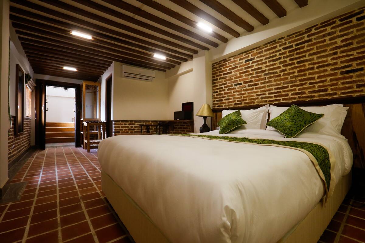 Quarto de hotel com uma cama grande, parede de tijolos e teto de madeira.