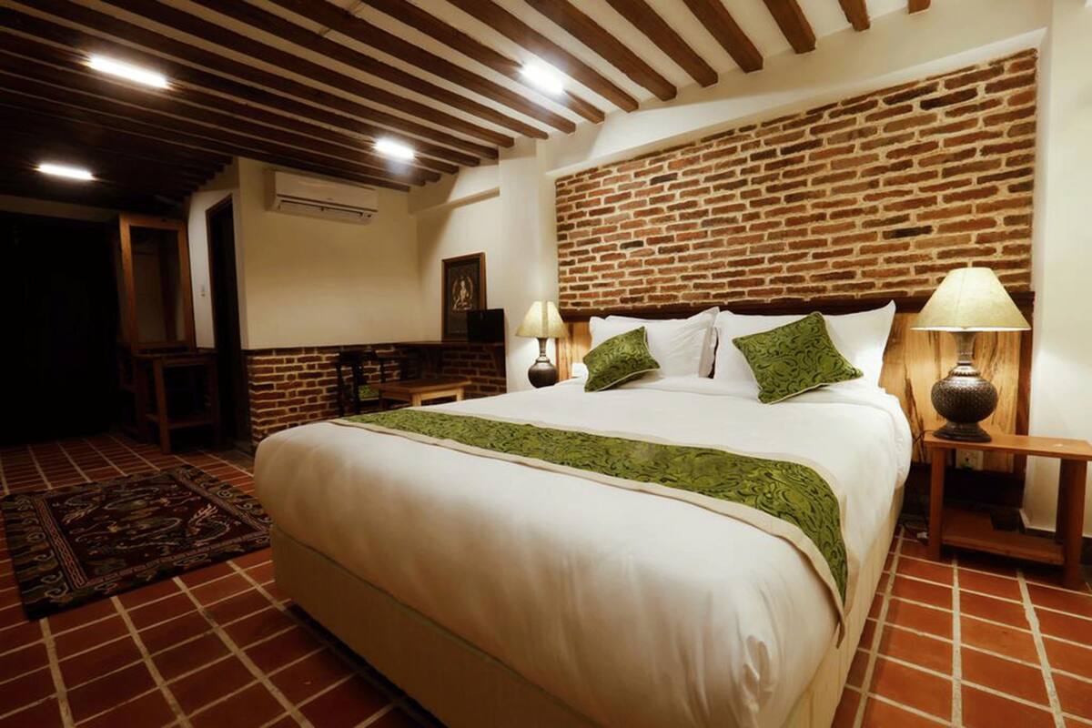 Um quarto com cabeceira de tijolos, uma cama grande com roupa de cama branca, duas luminárias de mesa e um tapete estampado no chão.