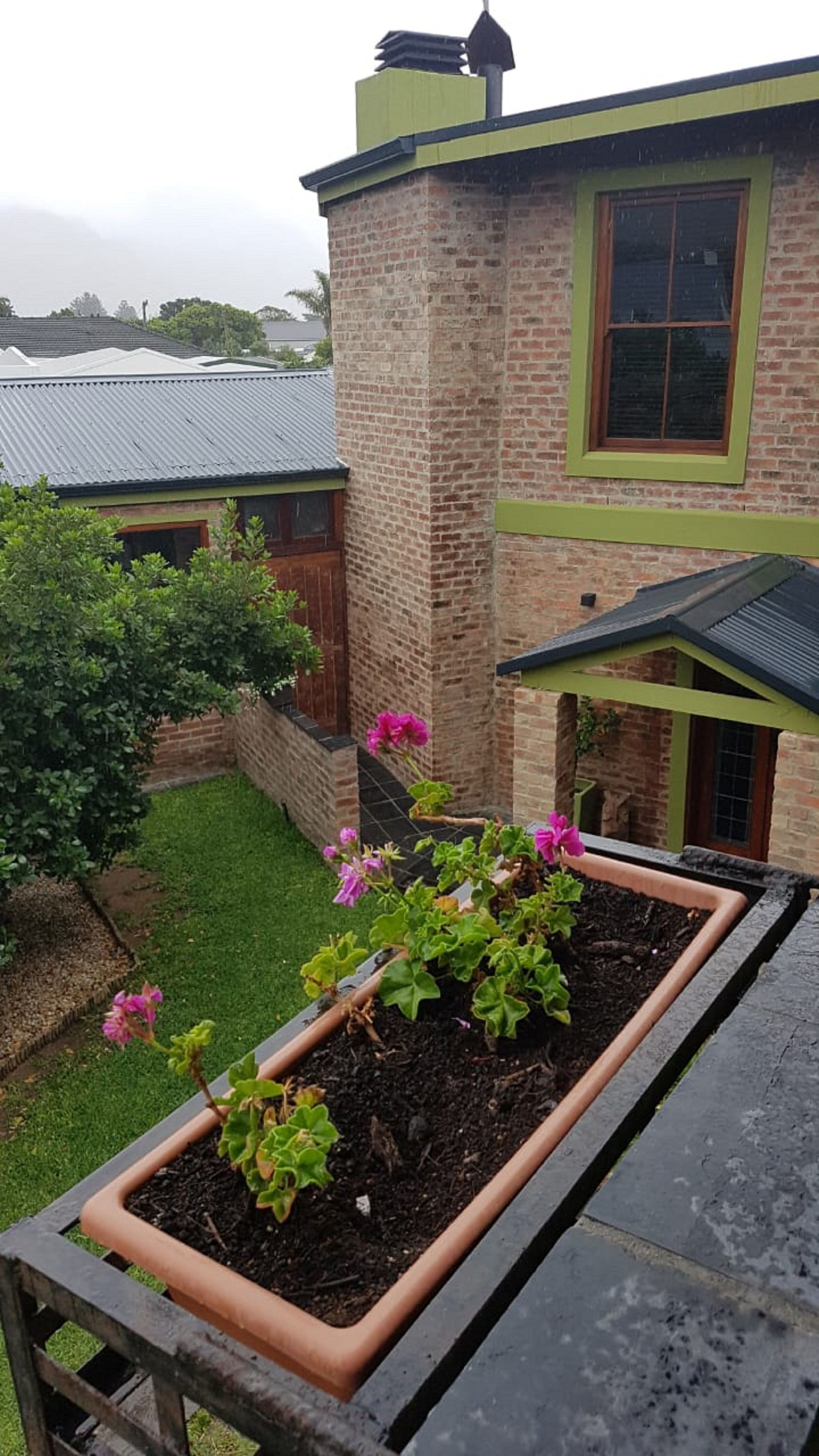 Uma casa de tijolo com telhado verde e um canteiro com flores cor-de-rosa.