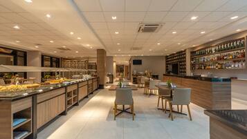 Um hall de hotel moderno com um balcão de recepção extenso, diversas áreas de estar e um bar com uma variedade de garrafas de bebidas alcoólicas.