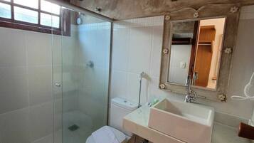 Uma casa de banho com cabine de chuveiro em vidro, sanita, lavatório com espelho e teto de madeira.