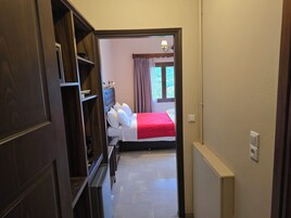 Quarto de hotel com cama, janela com cortinas, radiador e porta que dá para um corredor.