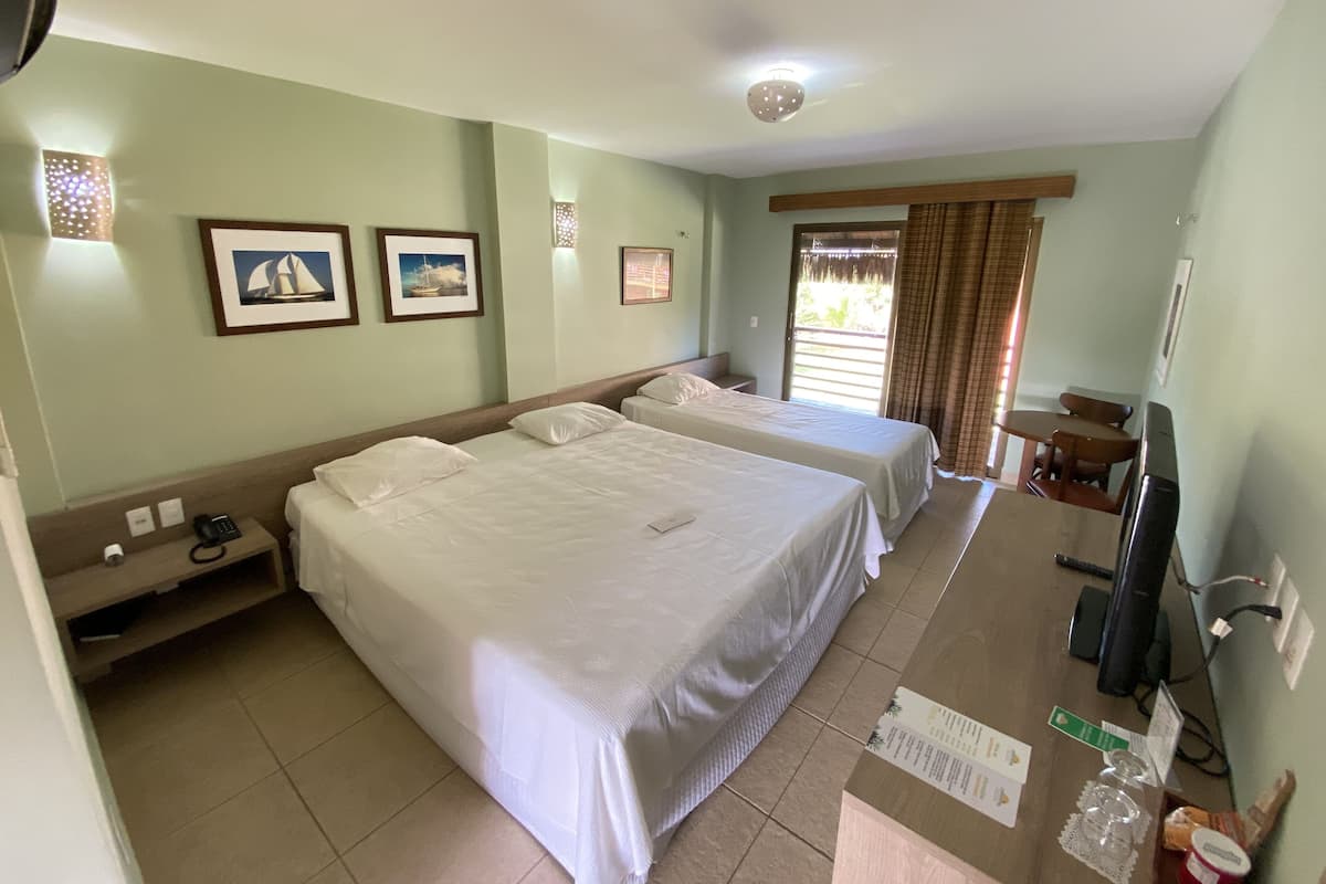 Quarto de hotel com duas camas, uma escrivaninha, televisão e uma janela com cortinas.