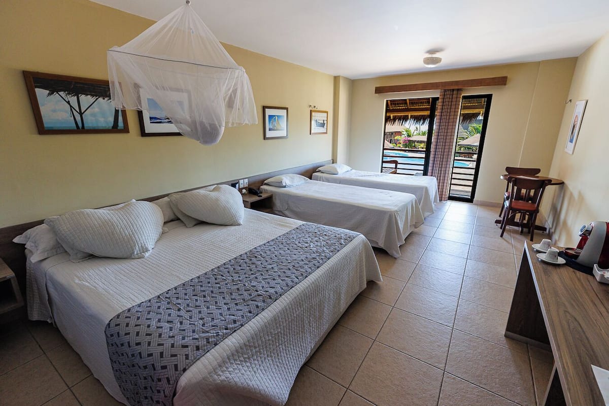 Quarto de hotel com duas camas, uma mesa, uma cadeira e varanda com vista.