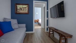 Uma sala de estar moderna com um sofá cinzento, um banco de madeira, uma TV montada e um quadro na parede.