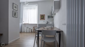 Uma cozinha moderna com armários brancos, uma mesa de jantar com cadeiras e uma janela com cortinas leves.