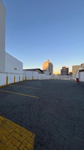 Uma área de estacionamento no terraço, com céu claro, superfície pavimentada e um edifício branco à esquerda.