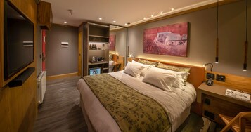 Quarto de hotel com uma cama grande, televisão, minibar e um quadro na parede.