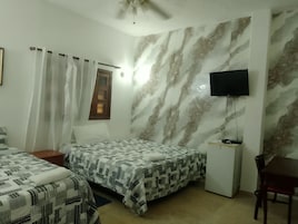 Quarto com duas camas, televisão e escrivaninha.