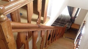 Uma escada de madeira com corrimão leva a um quarto com cama e janela.