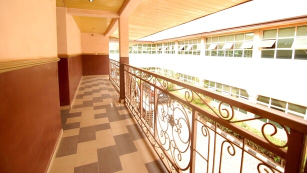 Um corredor com piso xadrez, corrimão de metal e vista para um edifício com várias janelas.