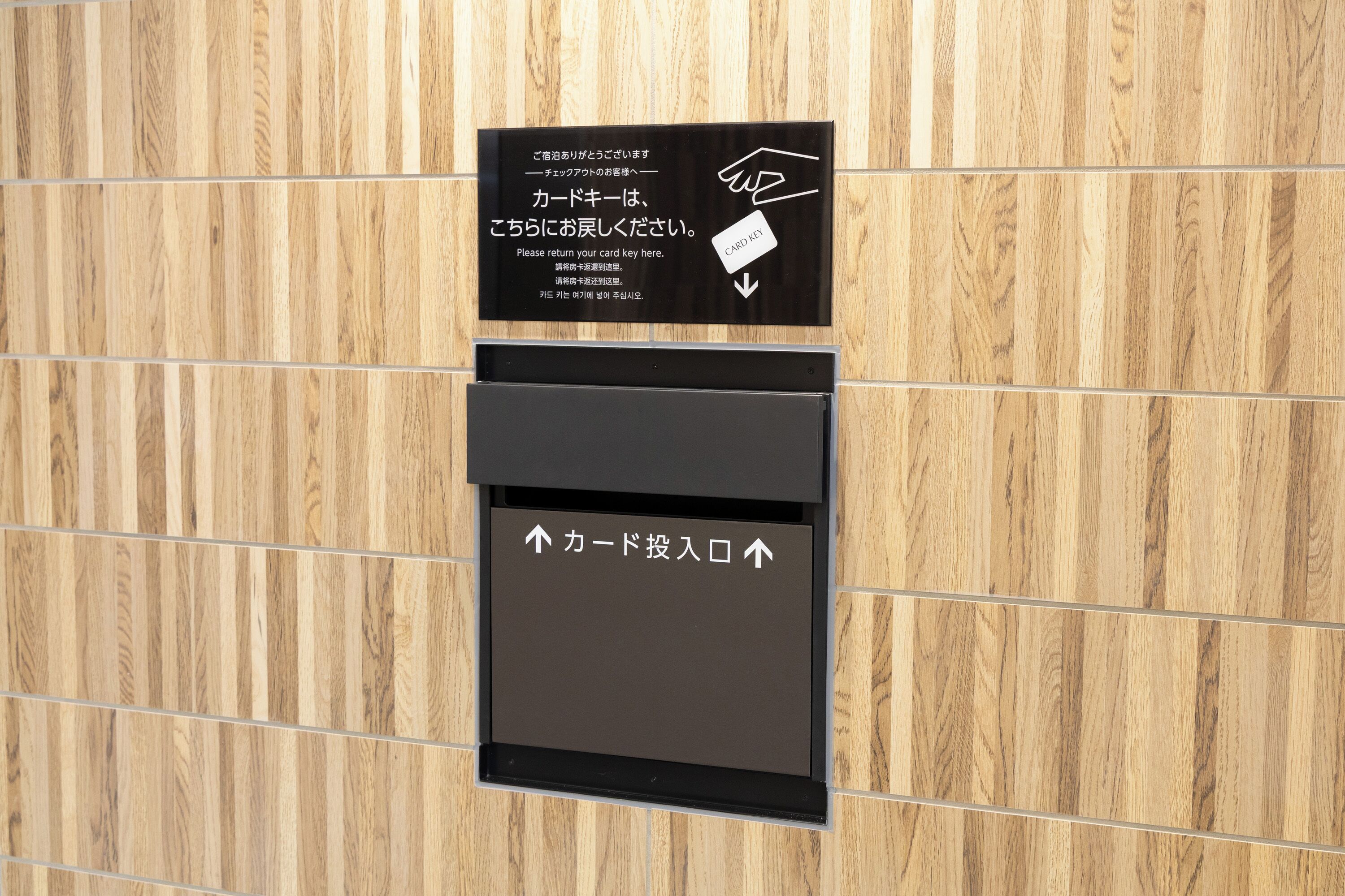 Leitor de cartão fixado na parede, com instruções em japonês e uma seta apontando para cima.