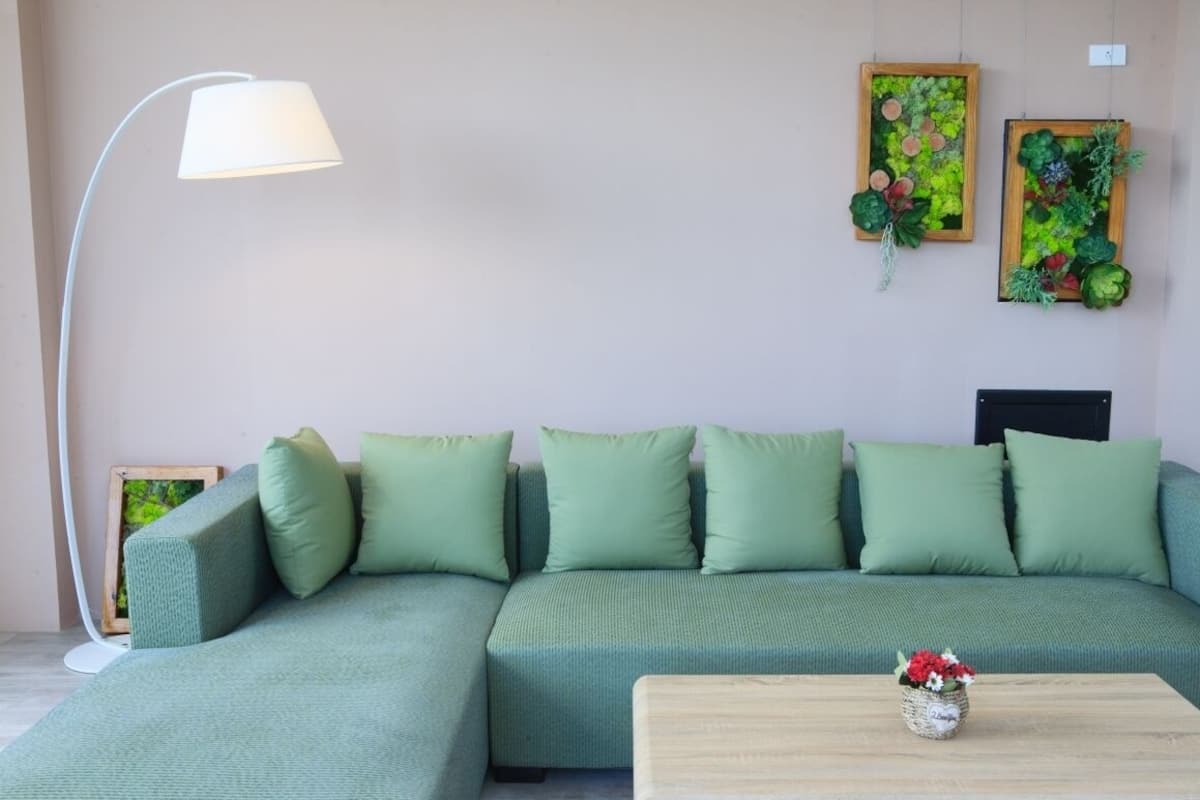 Um sofá verde com almofadas combinando, uma mesa de centro de madeira com um vaso de flores e um abajur.